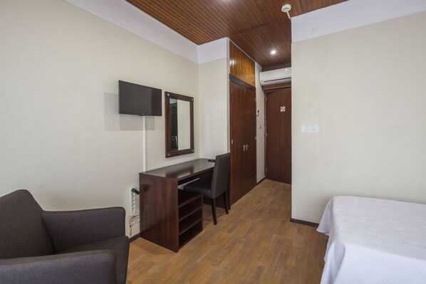Quarto de hotel com teto de madeira, escrivaninha com cadeira, televisão, guarda-roupa e uma cama.