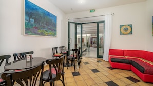 Um saguão de hotel com um sofá vermelho, uma área de refeições com mesa e cadeiras, e uma pintura na parede.