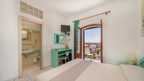 Quarto com cama, escrivaninha, cadeira, televisão e varanda com vista.