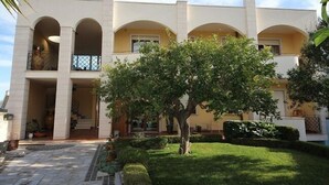 Um edifício de dois andares com fachada simétrica, janelas em arco e uma árvore central no pátio.
