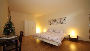 Quarto com cama, luminárias laterais, uma pequena árvore de Natal e um guarda-roupa.