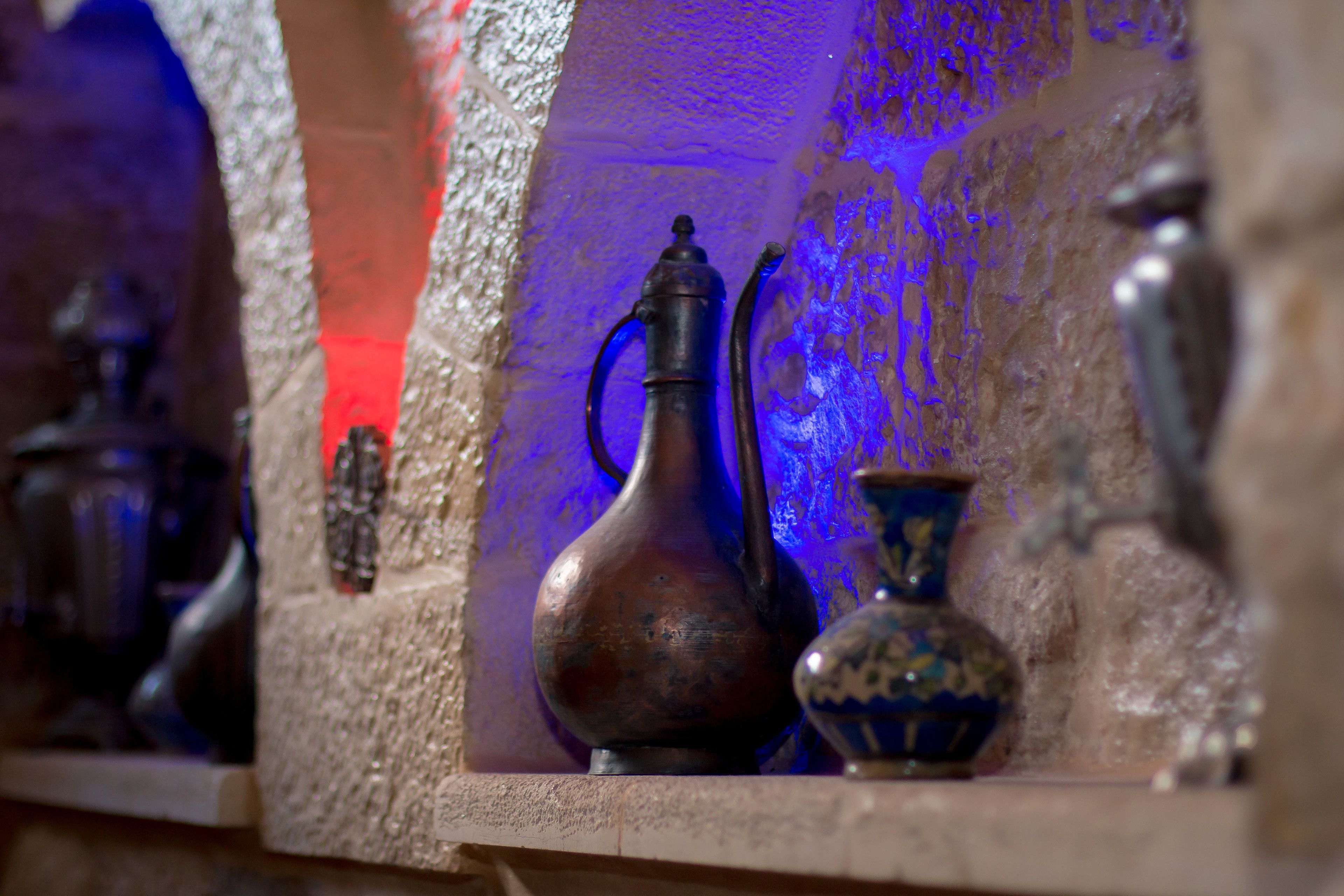 Uma parede de pedra com uma jarra de metal e um pequeno vaso azul.