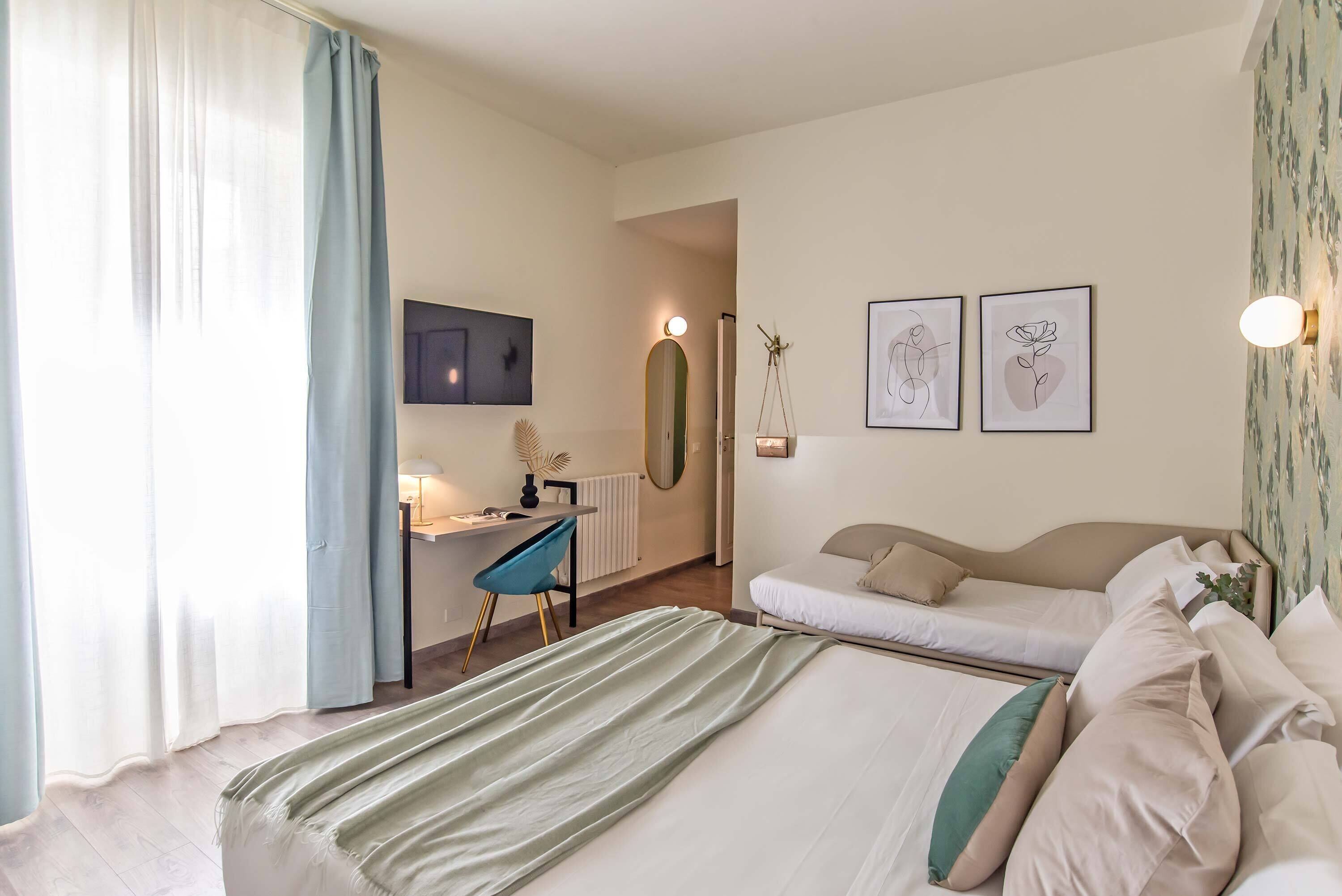 Quarto de hotel com uma cama grande, uma escrivaninha com cadeira, um pequeno sofá e obras de arte nas paredes.