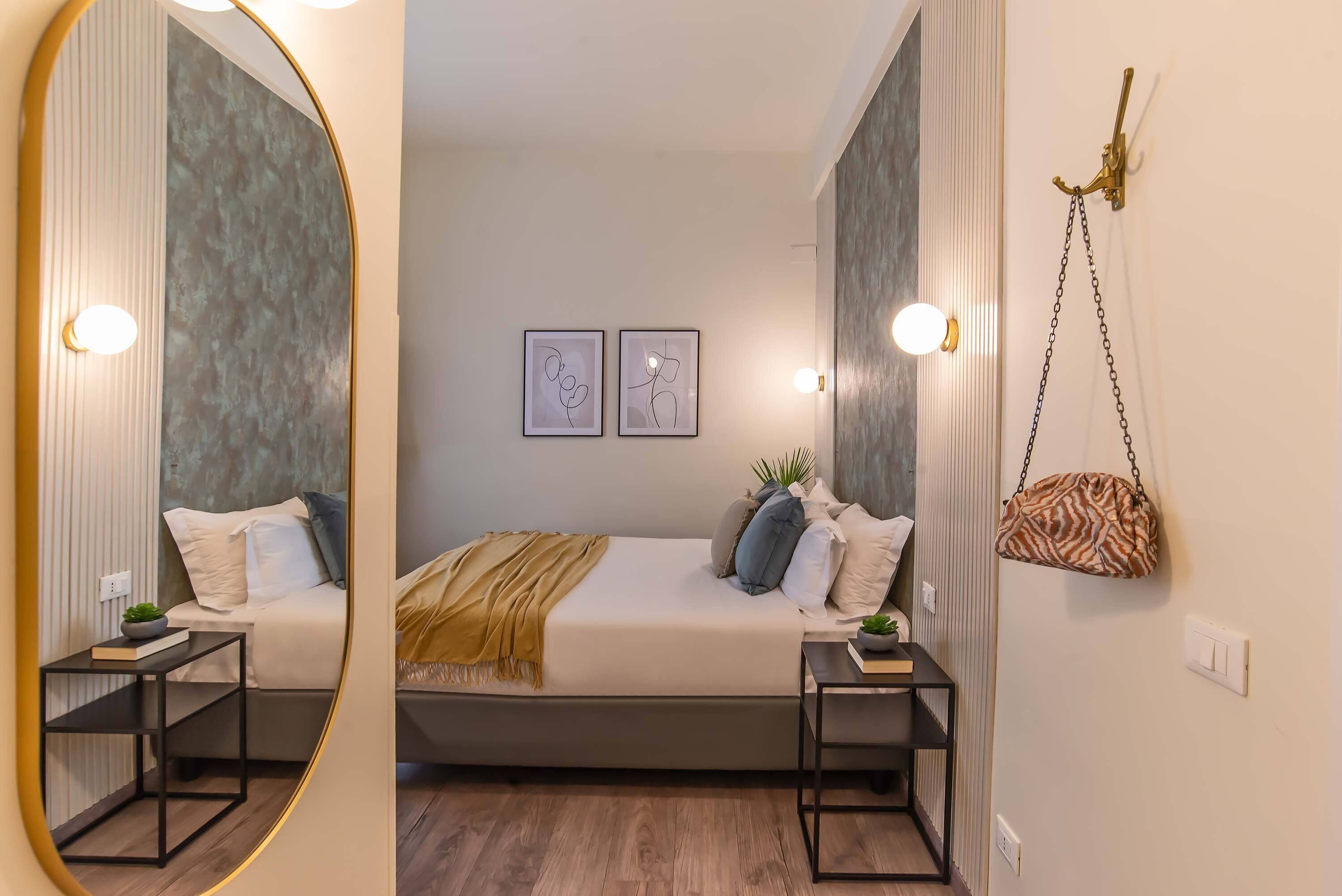 Quarto moderno com cama, mesas de cabeceira, espelho, decoração na parede e um acessório pendurado.