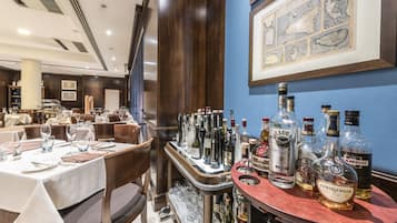 Uma área de bar com garrafas de bebidas alcoólicas organizadas, um balcão de bar bem abastecido e uma sala de jantar com mesas preparadas para hóspedes.