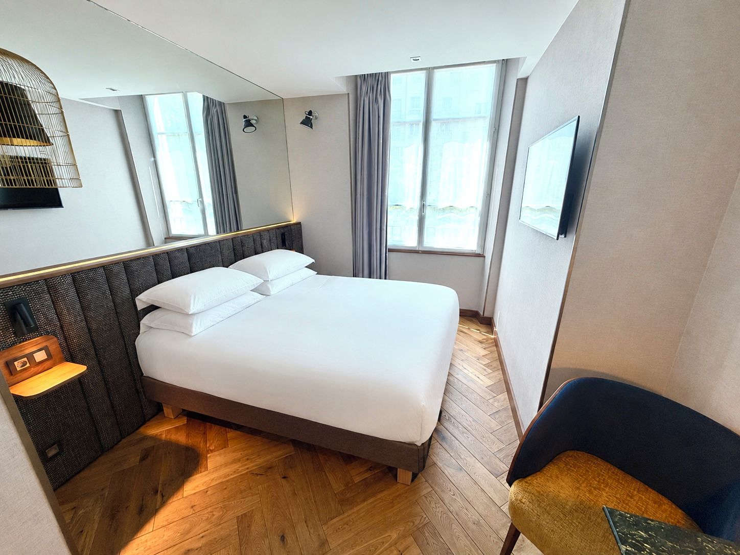 Quarto de hotel com cama, poltrona, televisão e janela.