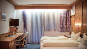 Quarto de hotel com escrivaninha de madeira, duas camas, televisão e janela com cortinas.