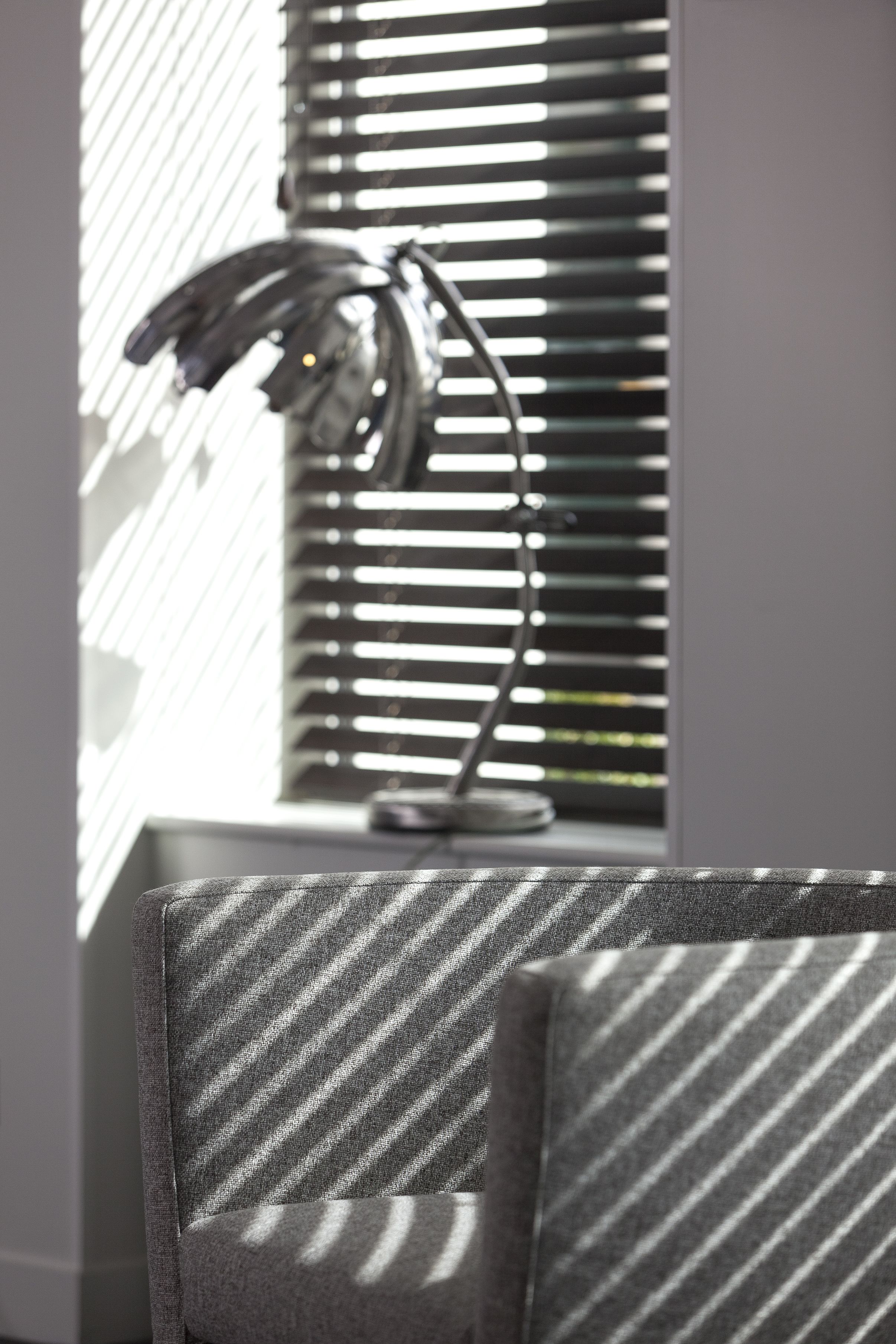 Uma cadeira com padrão listrado, uma luminária de metal e persianas horizontais ao fundo.
