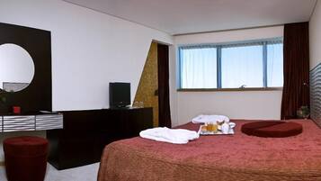 Quarto de hotel moderno com uma cama grande, televisão de tela plana, cômoda e janela com cortinas.