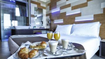 Quarto de hotel com cama, bandeja de café da manhã com croissants, suco e café, uma mesinha de cabeceira e um design de parede moderno.