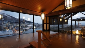 Um quarto espaçoso com piso de madeira, grandes janelas com vista para a cidade e um candeeiro tradicional pendurado no teto.