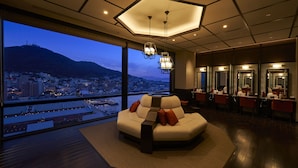 Quarto de hotel moderno com uma janela ampla que oferece vista para a cidade, um espaço de estar confortável e uma receção bem iluminada.