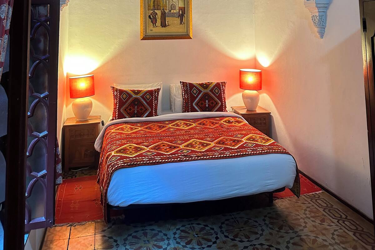 Quarto com cama, duas luminárias de cabeceira, ar condicionado fixado na parede e um arco decorativo.