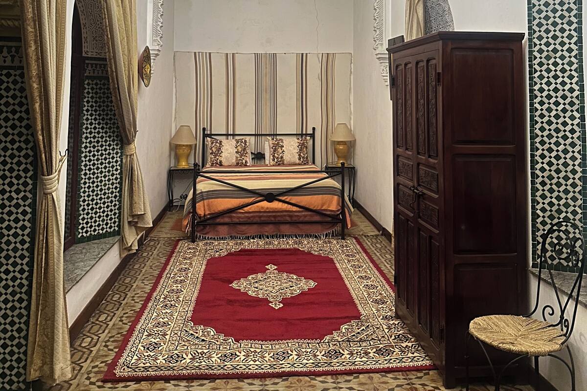Quarto com cama, luminária de cristal, armário e paredes estampadas.