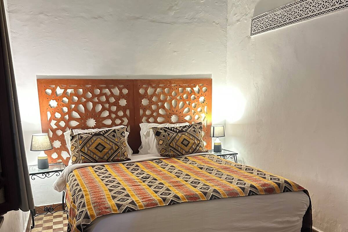 Uma cama com um cobreleito estampado, uma cabeceira decorativa e um tapete estampado no chão.