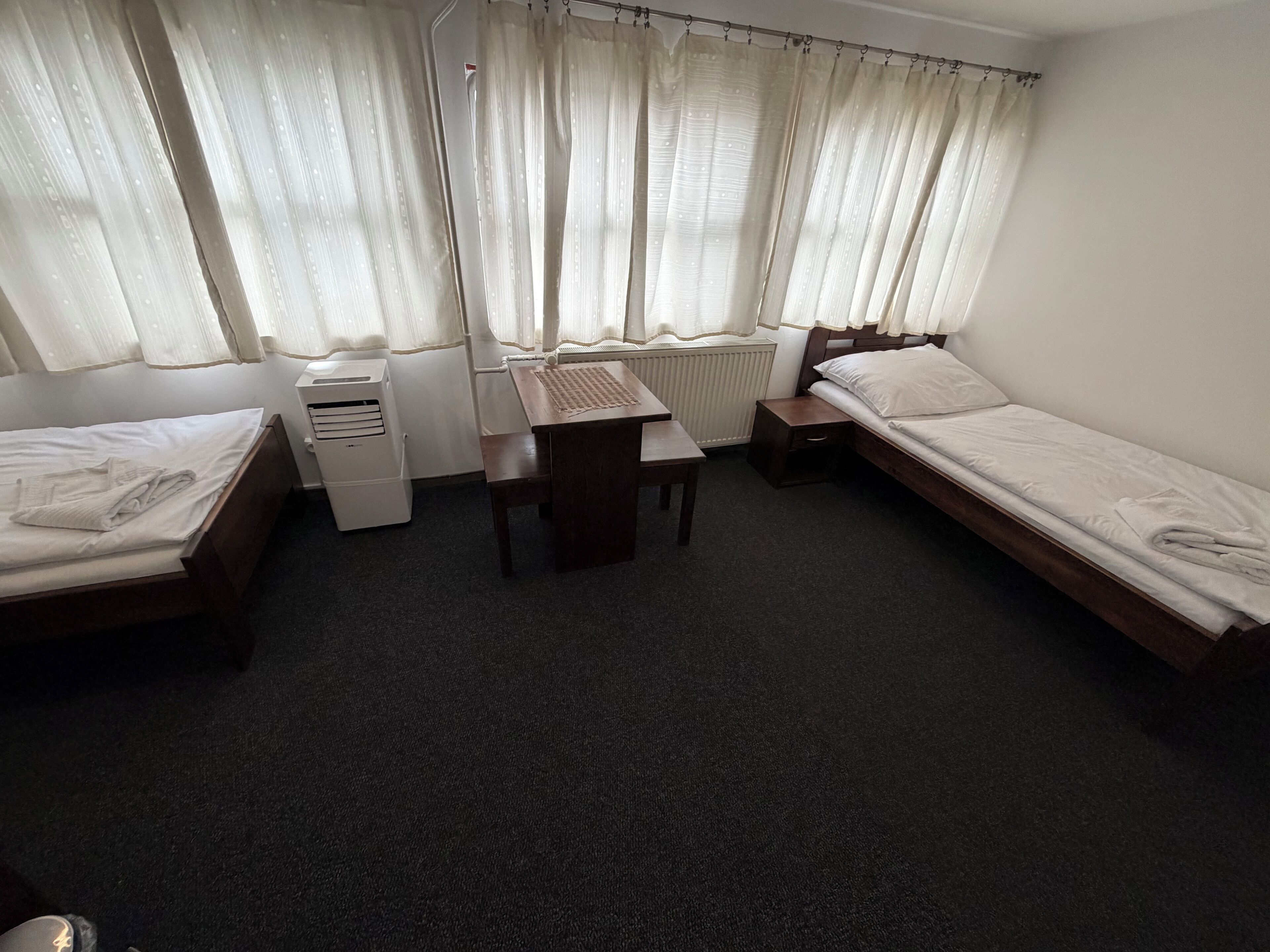 Quarto de hotel com duas camas de solteiro, uma escrivaninha, uma cadeira, um radiador e um aquecedor.