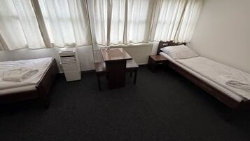 Quarto de hotel com duas camas de solteiro, uma escrivaninha, uma cadeira, um radiador e um aquecedor.