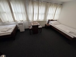 Quarto de hotel com duas camas de solteiro, uma escrivaninha, uma cadeira, um radiador e um aquecedor.
