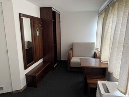 Quarto compacto com um guarda-roupa de madeira, um banco, um sofá e uma pequena mesa.