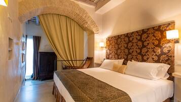 Quarto de hotel com uma cama grande, cabeceira de madeira, uma cadeira e uma janela com cortinas.