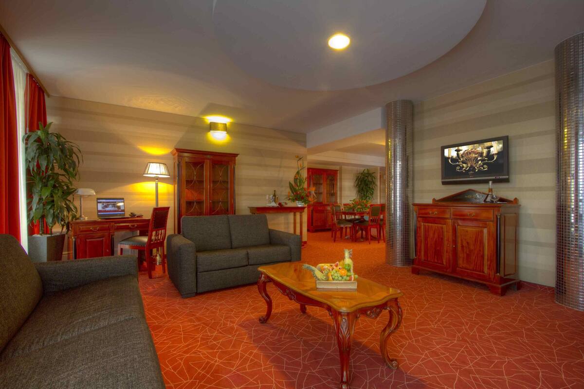 Um hall de hotel com sofá, poltrona, mesa de jantar, televisão e uma planta.