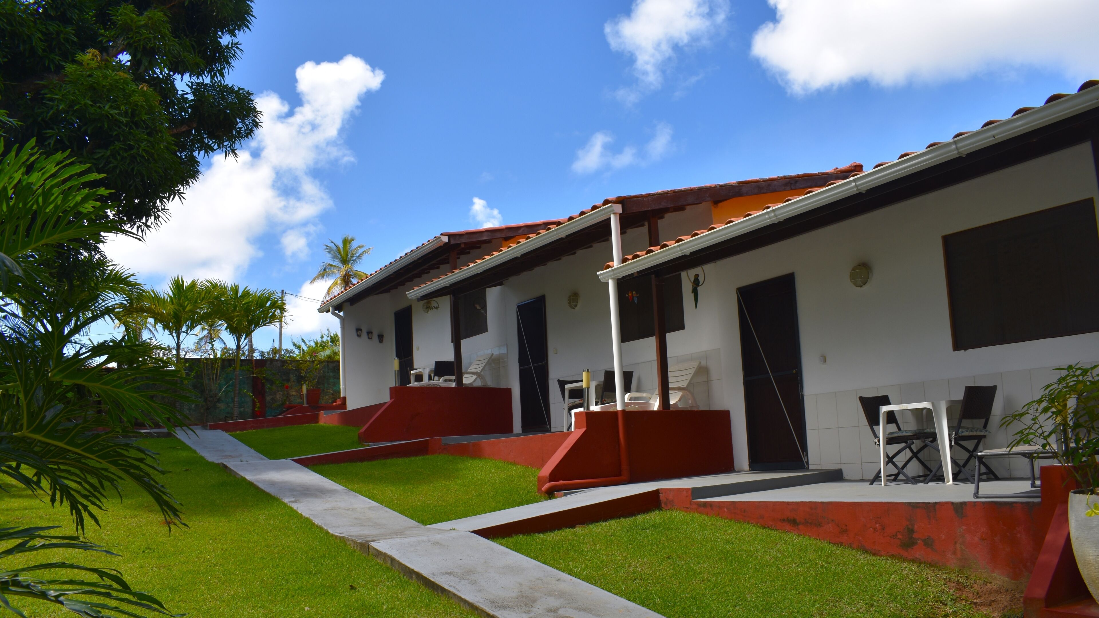 Um edifício de dois andares com fachada vermelha e branca, um alpendre com área de estar externa e um gramado bem cuidado.