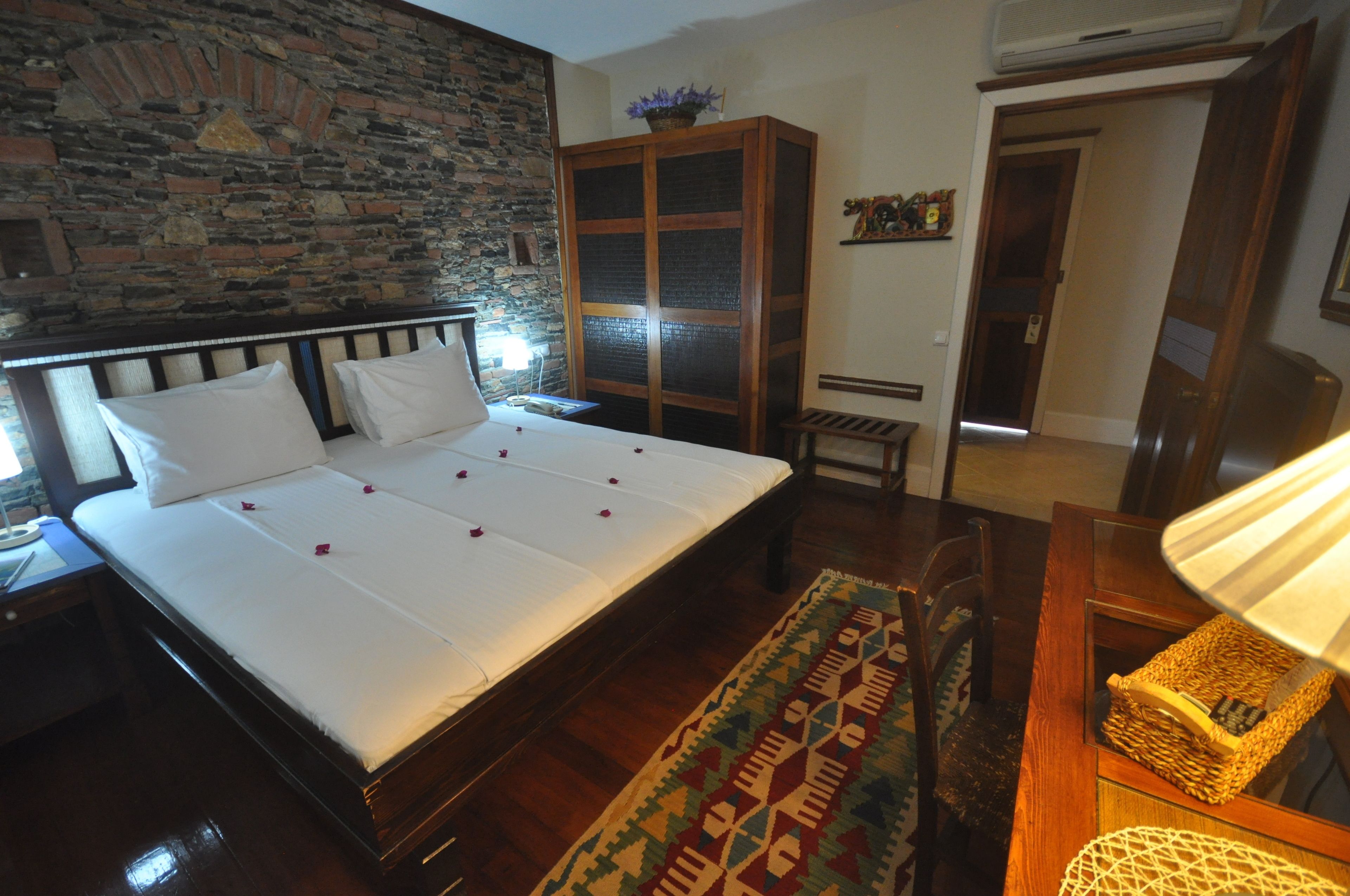 Um quarto com uma cama grande, uma parede de pedra, um armário de madeira e um tapete estampado.