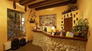 Uma área de recepção com parede de pedra, vigas de madeira no teto, um espelho grande e diversos objetos decorativos, incluindo máscaras e um mapa-múndi.