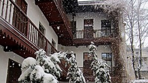 Um edifício coberto de neve com varanda e árvores carregadas de neve.
