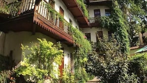 Um edifício tradicional de dois andares com varandas, rodeado por vegetação exuberante e um caminho no jardim.