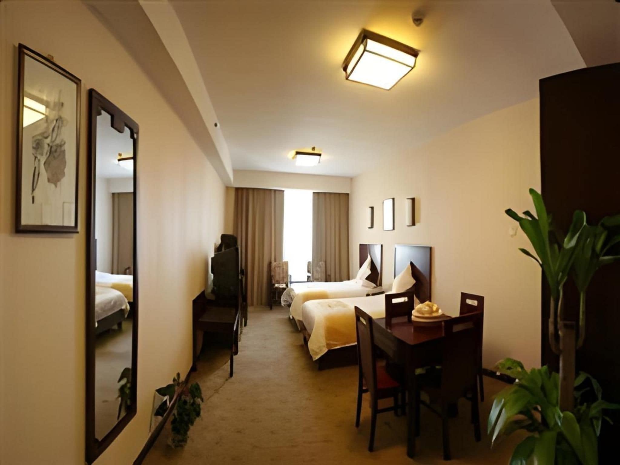 Quarto de hotel com duas camas, uma escrivaninha com cadeiras, um espelho e uma planta.