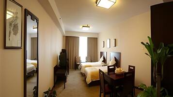 Quarto de hotel com duas camas, uma escrivaninha com cadeiras, um espelho e uma planta.