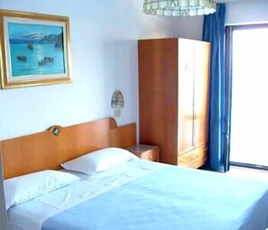 Quarto de hotel com cama, guarda-roupa de madeira, um quadro na parede e janela com cortinas.