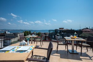 Terraço no telhado com mesas e cadeiras, com vista para a paisagem urbana e o mar.
