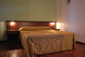 Uma cama de solteiro com cabeceira de madeira, duas luminárias de apoio e uma mesa de cabeceira com gaveta.