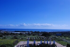 Estrutura de concreto com um pérgola em primeiro plano, com vista para uma paisagem costeira sob um céu claro.