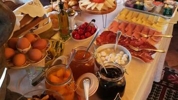 Buffet com diversos alimentos, incluindo pães, queijos, carnes, frutas e acompanhamentos.