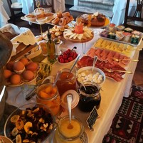 Buffet com diversos alimentos, incluindo pães, queijos, carnes, frutas e acompanhamentos.