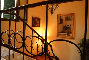 Uma escadaria com grades de metal decoradas, um candeeiro fixado na parede e obras de arte emolduradas.