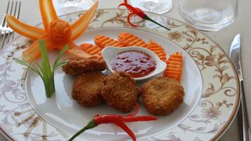 Um prato com petiscos empanados, cenouras e uma pequena tigela de molho, dispostos em um prato decorativo.