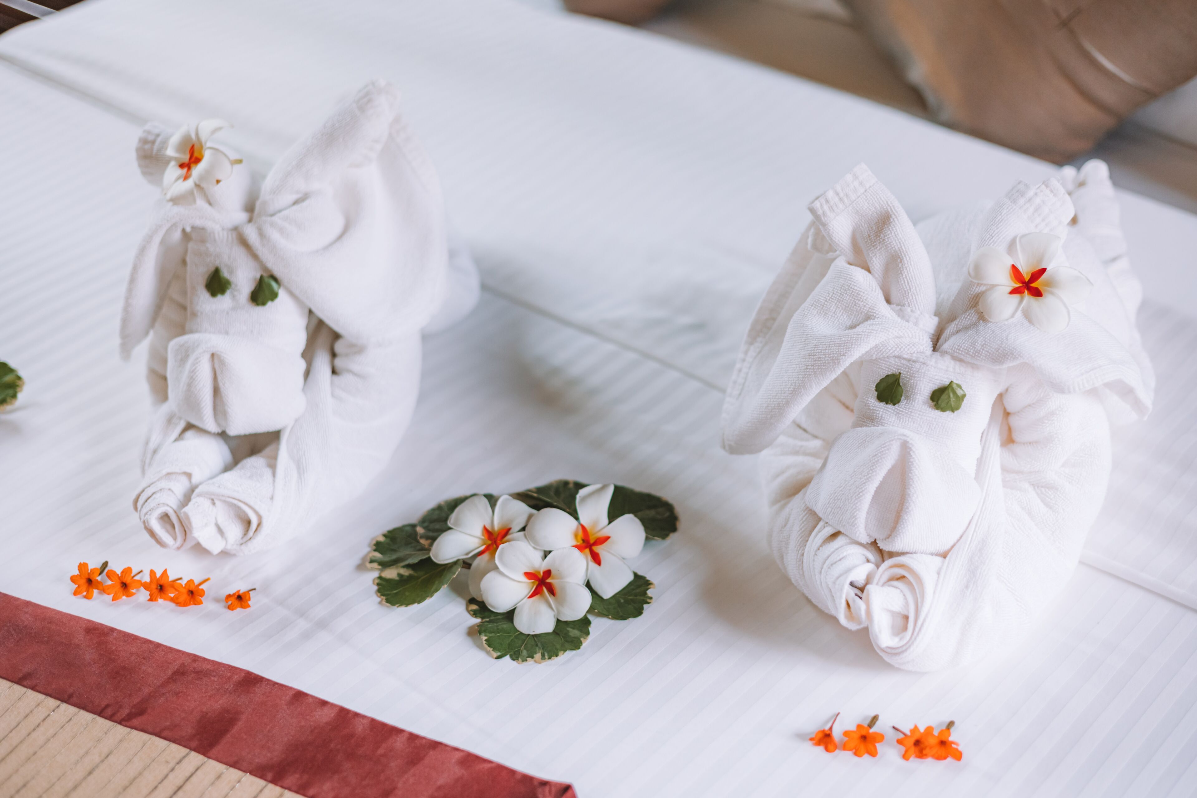 Duas toalhas brancas moldadas em formato de coelhos, com flores brancas e folhas verdes.