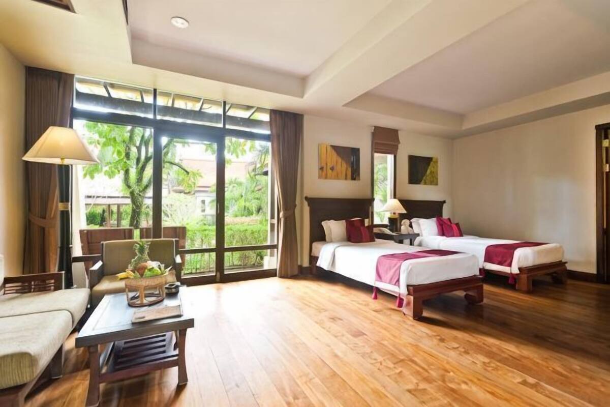 Quarto de hotel com duas camas, uma escrivaninha e uma janela grande.