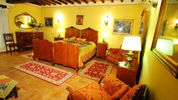 Quarto tradicional com cama de madeira, duas mesas de cabeceira com abajures, uma cadeira e uma pequena mesa com um vaso.