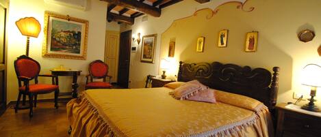 Quarto com cama grande, cabeceira de madeira e uma cadeira vermelha. Há uma pequena mesa com uma luminária e um quadro na parede.