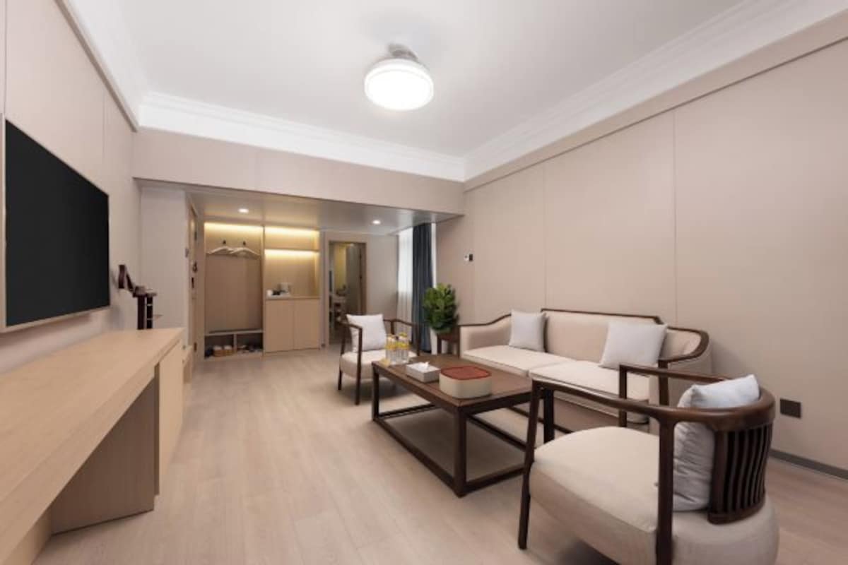Uma sala de estar moderna com sofá, mesa de centro e TV. Cozinha visível ao fundo.