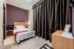Quarto de hotel com cama, mesa de cabeceira e escrivaninha com cadeira.