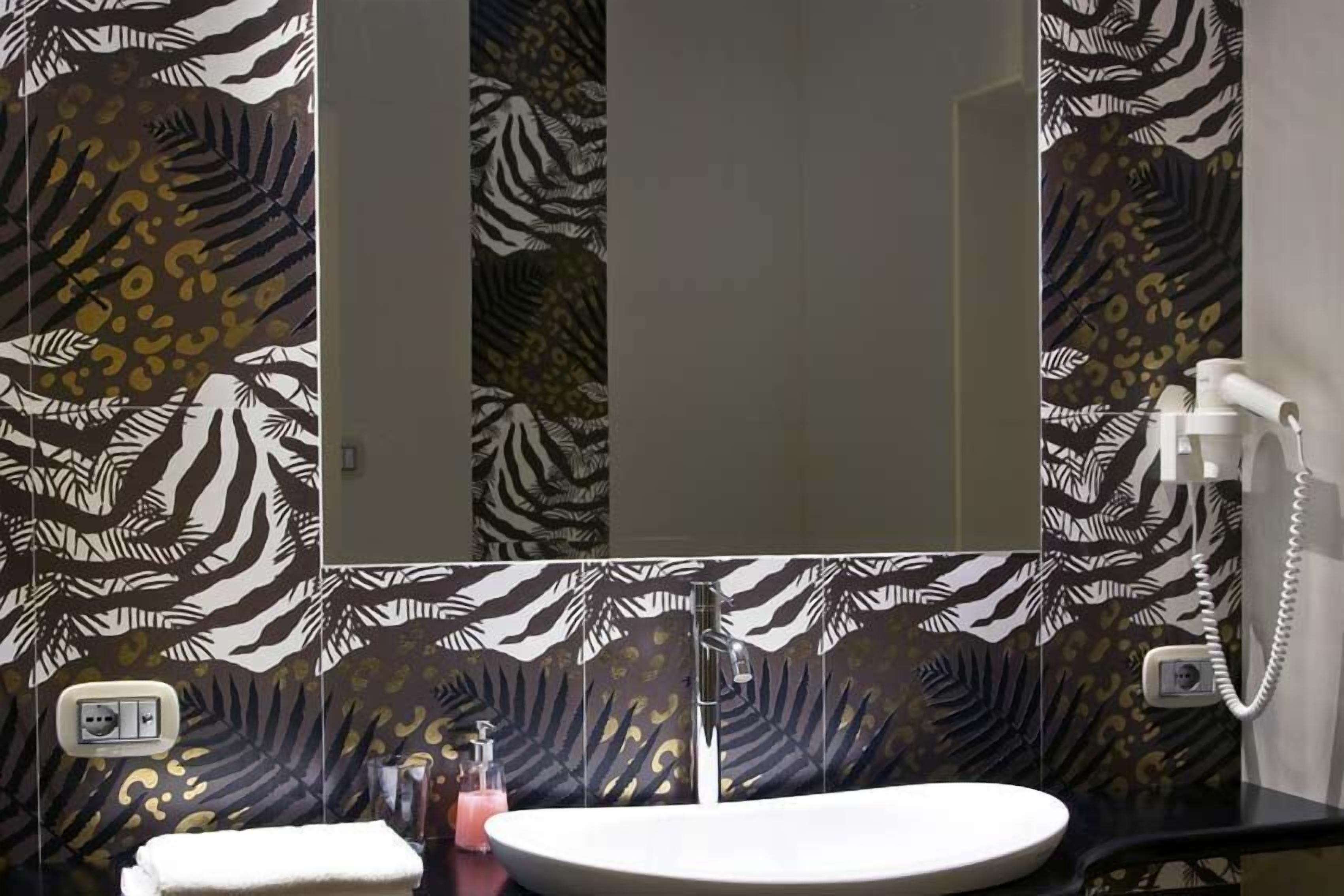 Casa de banho com parede de azulejos a listras de zebra, uma pia branca, um espelho e um telefone.