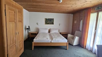 Um quarto com uma cama de madeira, um ventilador, uma cadeira e um quadro na parede.