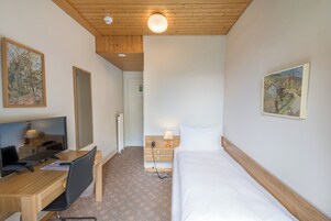 Quarto de hotel com escrivaninha de madeira, uma cama e duas pinturas nas paredes.