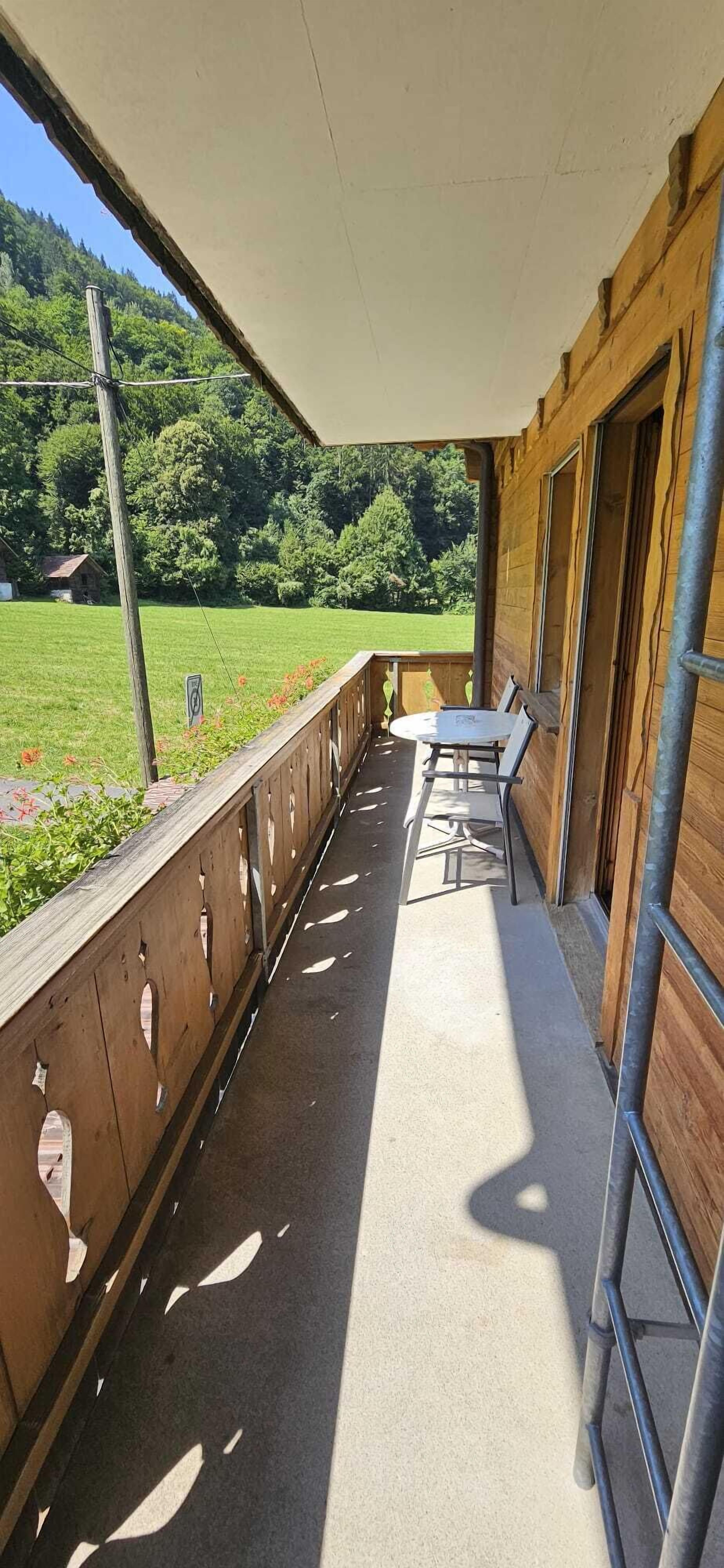 Um deck de madeira com área coberta, mobiliário para área externa e vista para um campo verde e árvores.